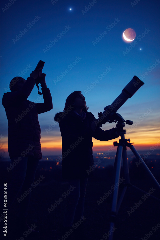 Mother and daughter observing stars, planets, Moon and night sky with ...