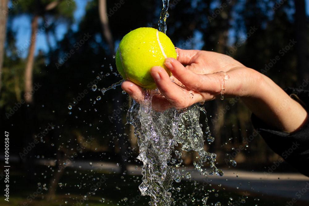 hand throws the tennis ball with water splashing around it. Water ...