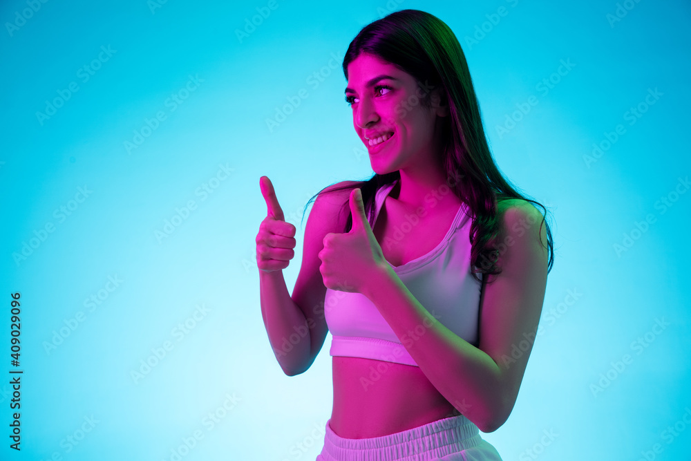 Smiling, thumbs up. Brunette woman's portrait isolated on blue studio ...