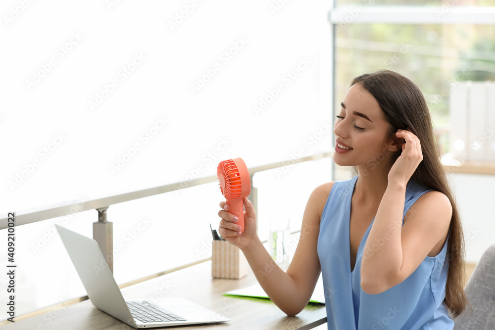 Young woman enjoying air flow from portable fan at workplace, space for ...