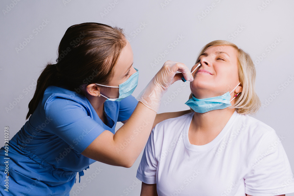 Young nurse in a medical mask takes a COVID 19 test from the nose of an ...