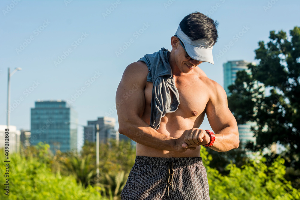 A shirtless and buff man wearing a sunvisor checks the time and ...