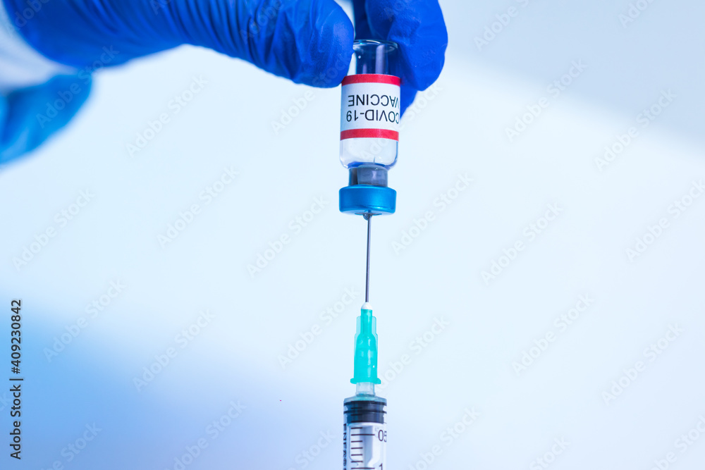 Doctor inserts the needle of a syringe into the vial with the COVID-19 ...