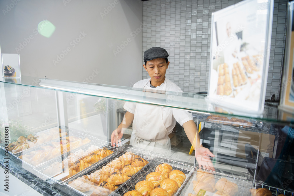 Male baker arranging fresh French pastries in bakery display case Stock ...