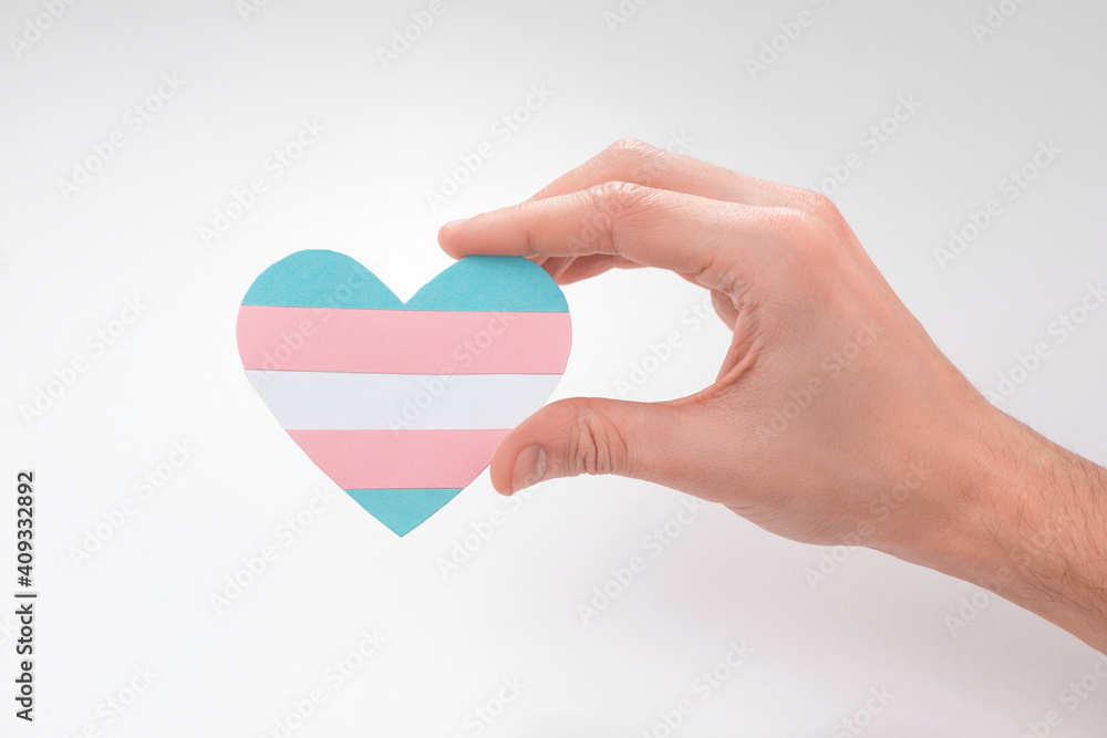 Hand holding a paper heart with transgender flag on white background ...