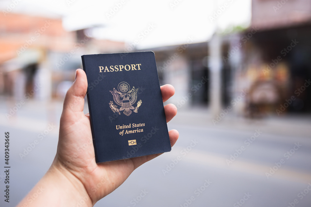 Human hand holding a blue American passport in front of a blurry ...