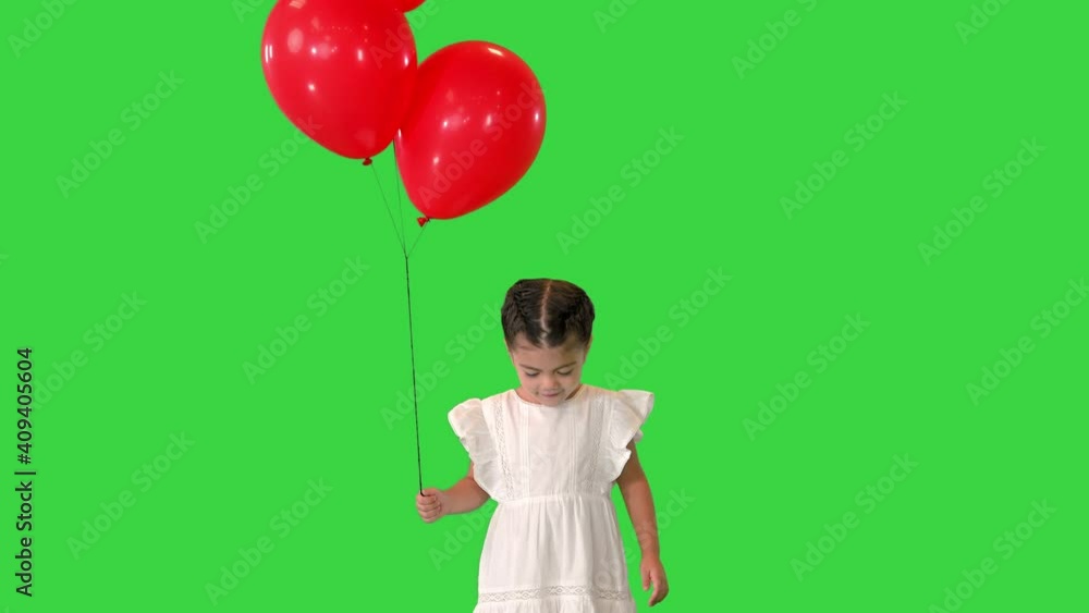 Adorable little girl holds tightly to a large bunch of helium balloons ...