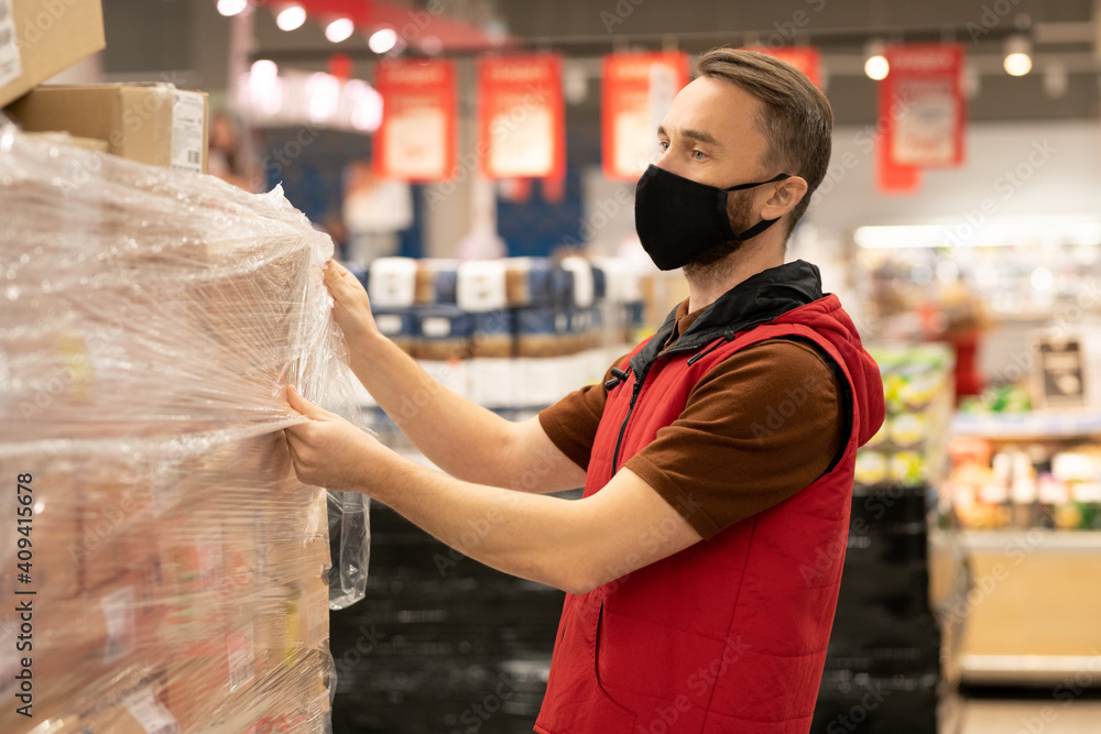 Young male worker of supermarket unpacking huge stack of packed boxes ...