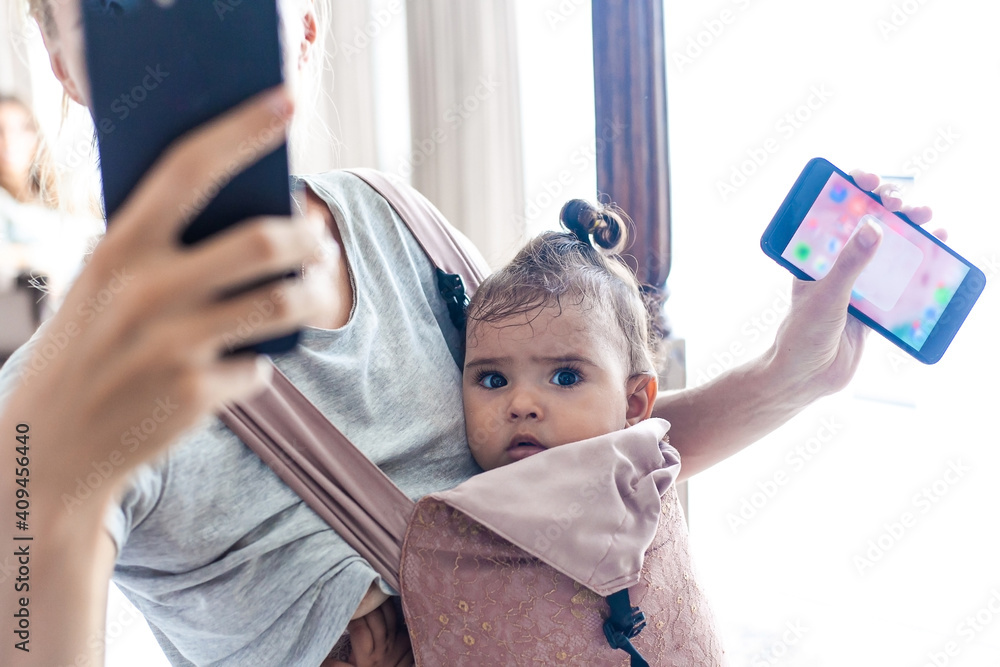 Indian toddler girl sits in a sling on her mother's chest, who is ...
