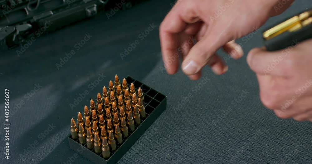 Close-up of male hands loading bullets into a gun magazine clip at a ...