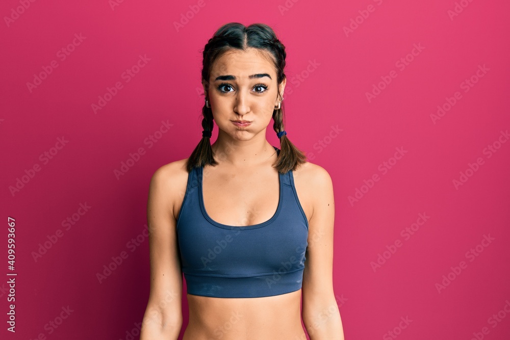 Young brunette girl wearing sportswear and braids puffing cheeks with ...