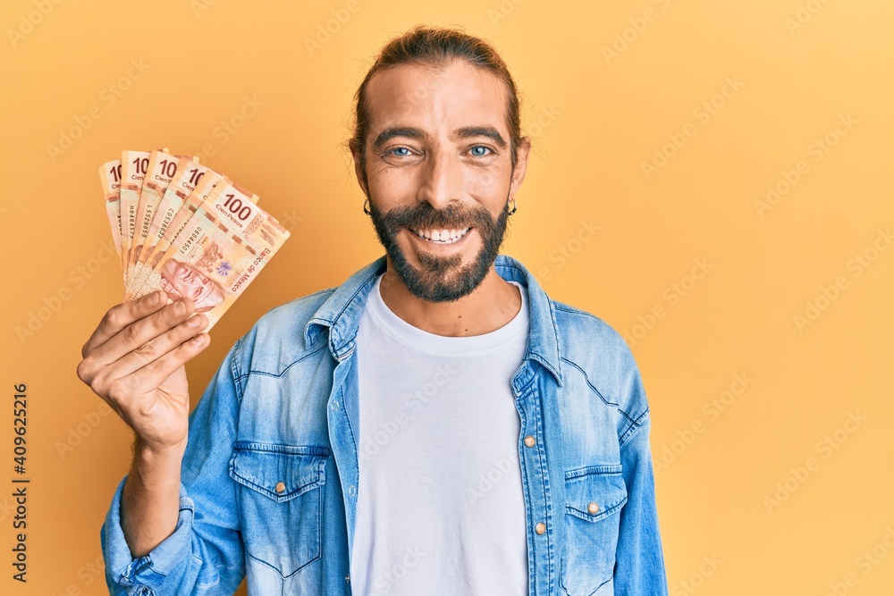 Attractive man with long hair and beard holding 100 mexican pesos ...