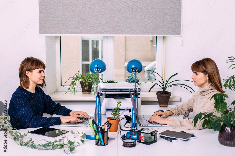 Two women twins are working opposite each other in the office on a ...