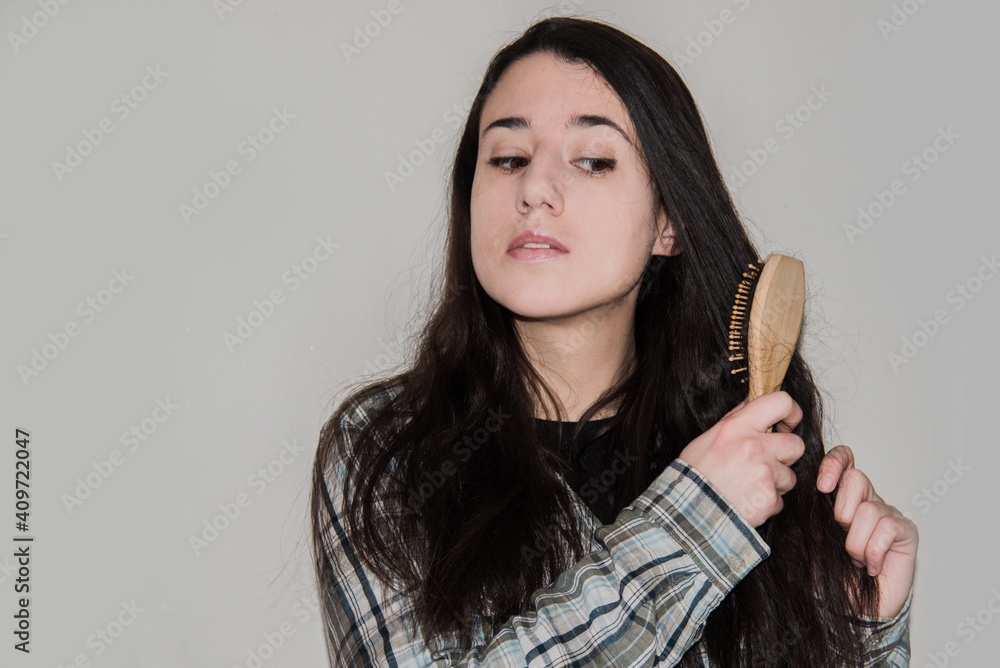 Mujer joven sujetando con la mano un cepillo con pelo caído mientras ...
