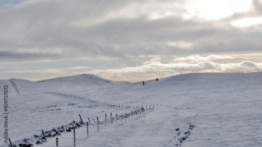 snowy hilly landscape with a fence, stone wall and silhouettes of two ...