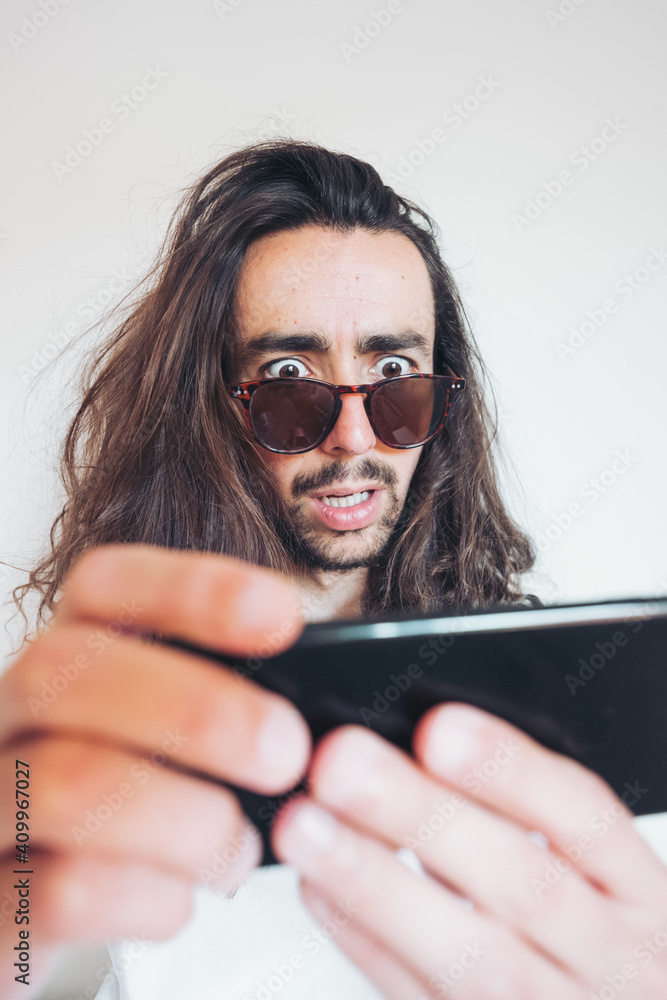 Overwhelmed young long haired hipster guy in sunglasses looking at ...
