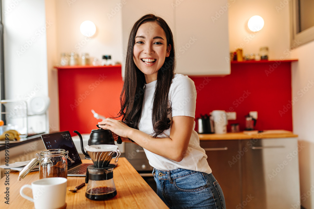Charming woman sincerely laughs and poses in kitchen. Asian girl making ...