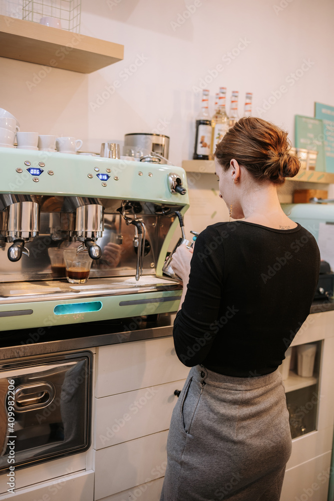 Side view of female cafe worker using coffee machine while preparing ...