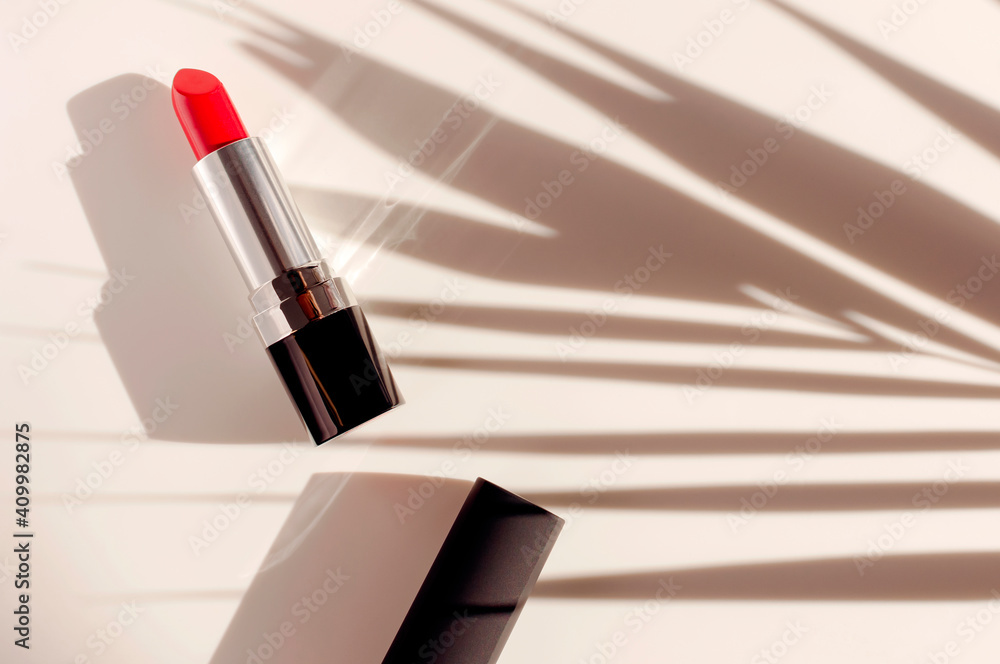 Red lipstick sun shadows from palm leaf on beige background flat lay ...