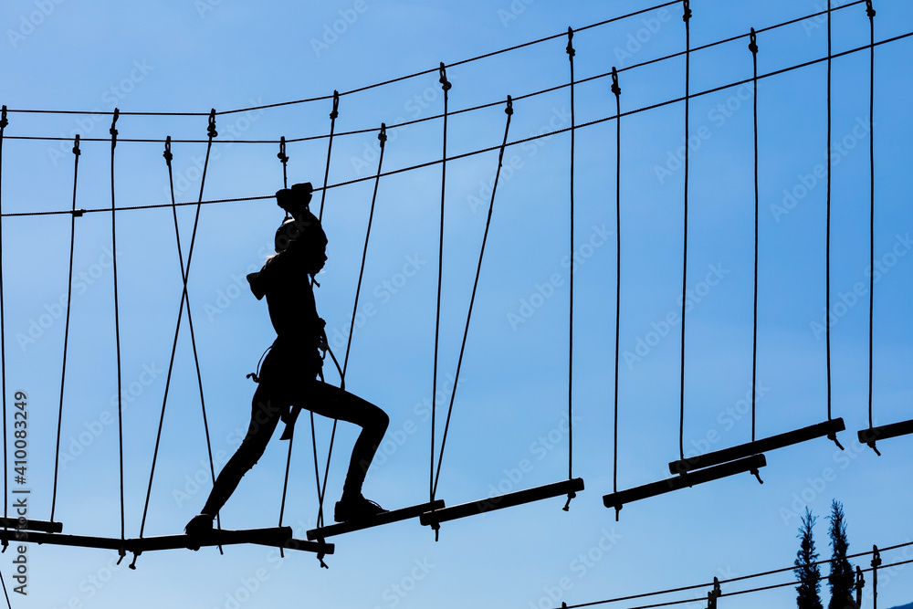 Silhouette of young girl in helmet climbing on high rope course against ...