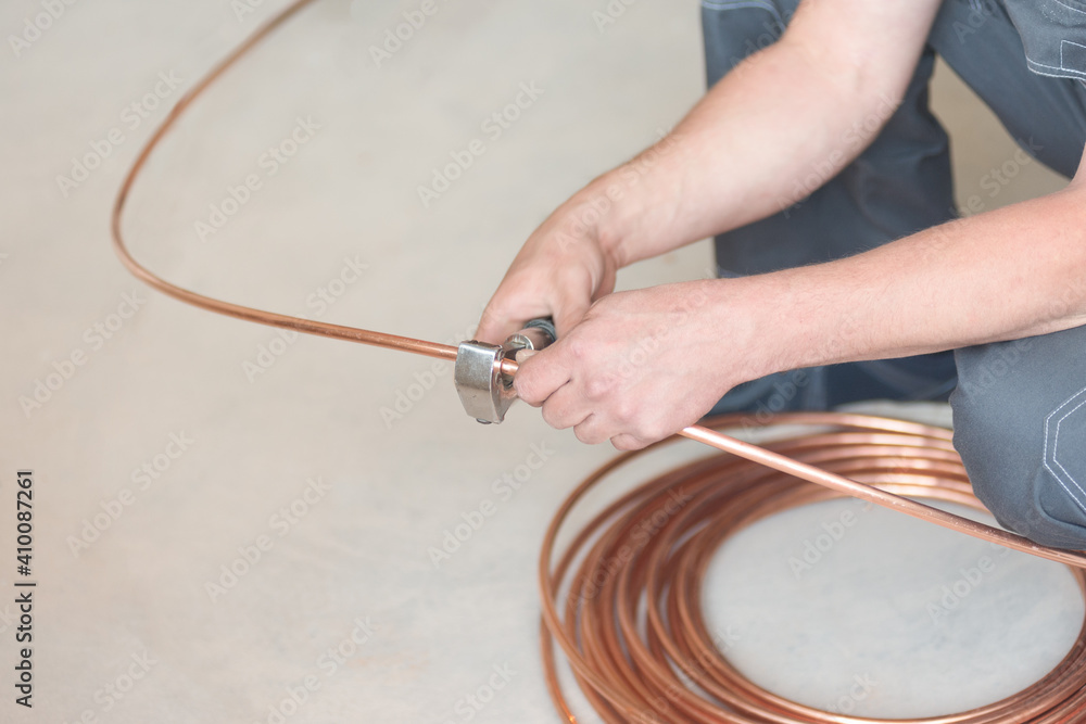 The worker cuts a copper tube with a cutter to connect the air ...