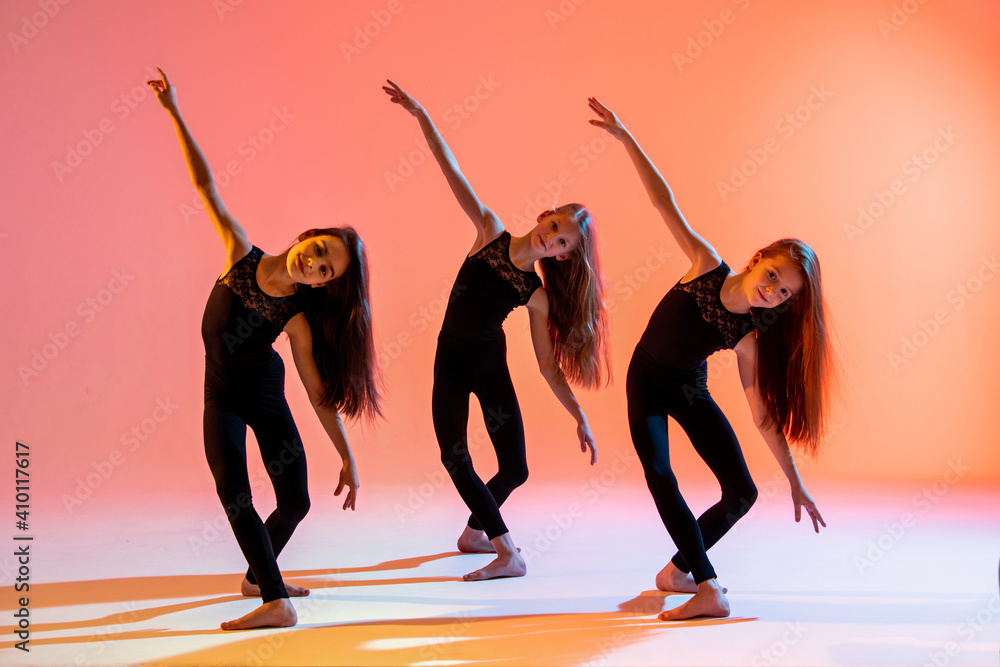 group of three ballet girls in black tight-fitting suits dancing on red ...