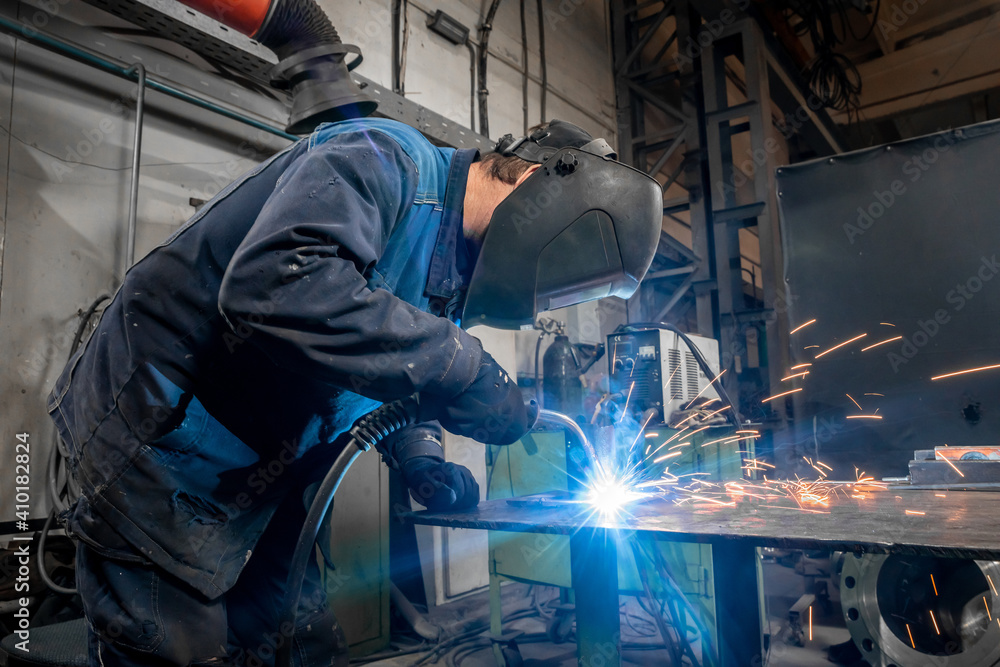 welding work at a metalworking plant. A helmeted welder welds a metal ...