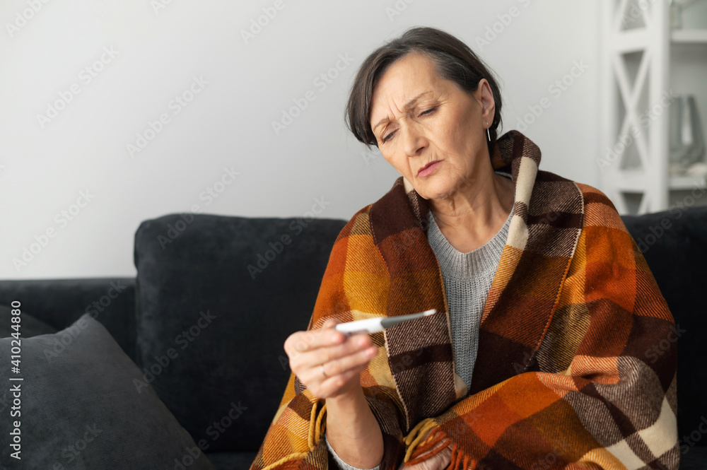 An older lady measures body temperature with a thermometer. Sick senior ...