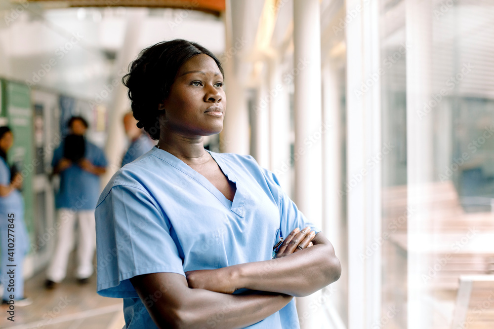 Contemplating female nurse with arms crossed looking through window in ...