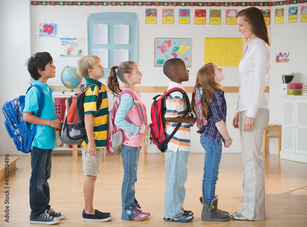 School children (8-9) with female teacher standing in row in classroom ...