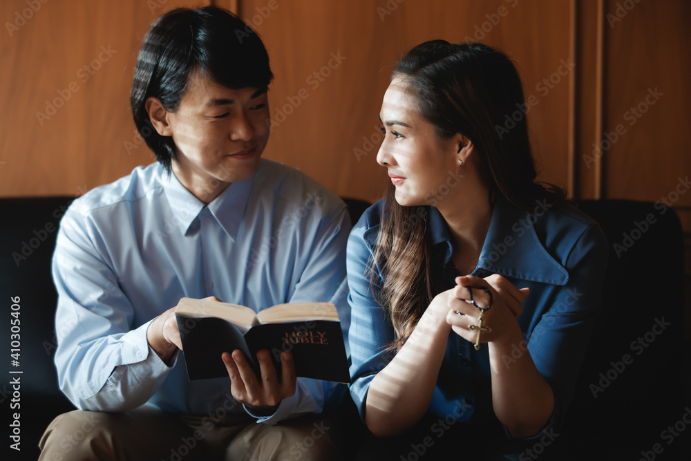 Asian man sitting teaching a Bible prayer to a Christian woman. As a ...