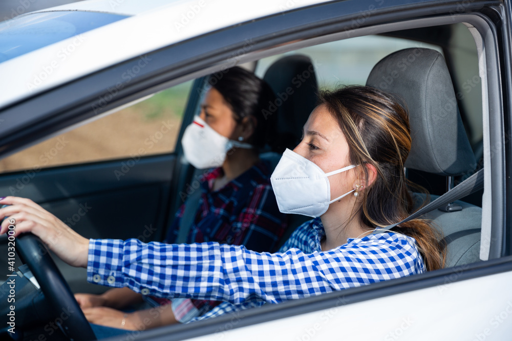 Young Hispanic woman in medical face mask driving car with female ...