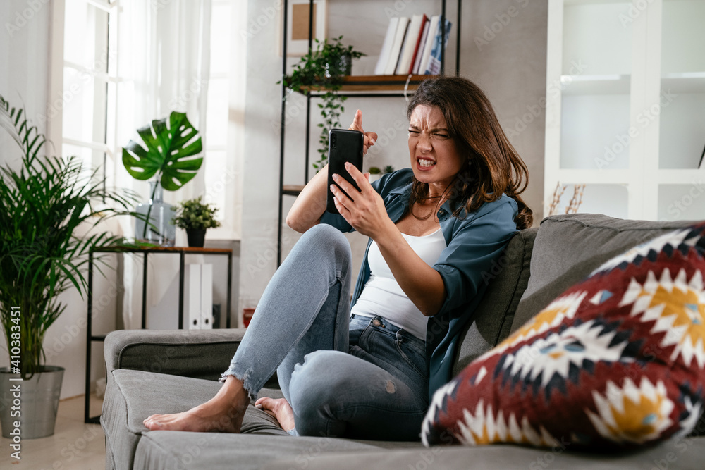 Sad woman sitting on the couch, using the phone. Upset woman waiting ...