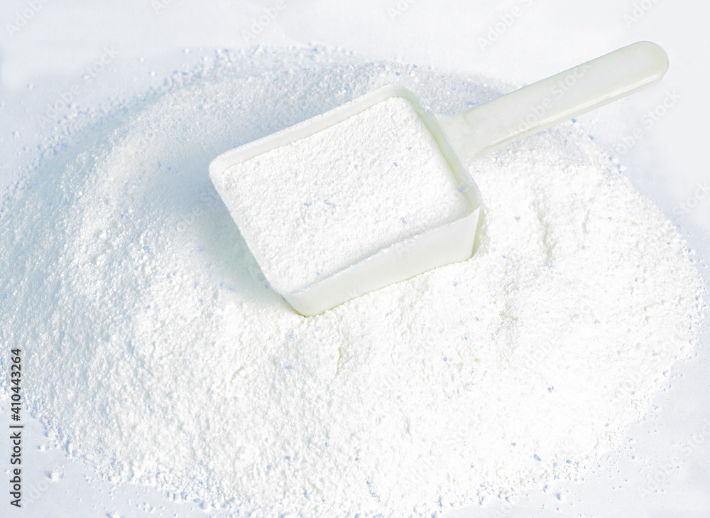 Close-up white detergent mixed with blue granules in white spoon used ...