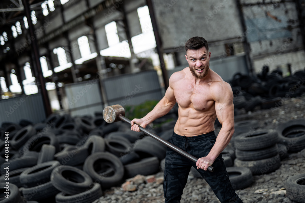 Muscle athlete strongman shirtless trying to hit a huge tyre with a ...