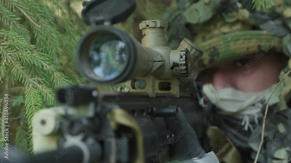 Closeup of disguised soldier aiming with sniper rifle sitting in ambush ...