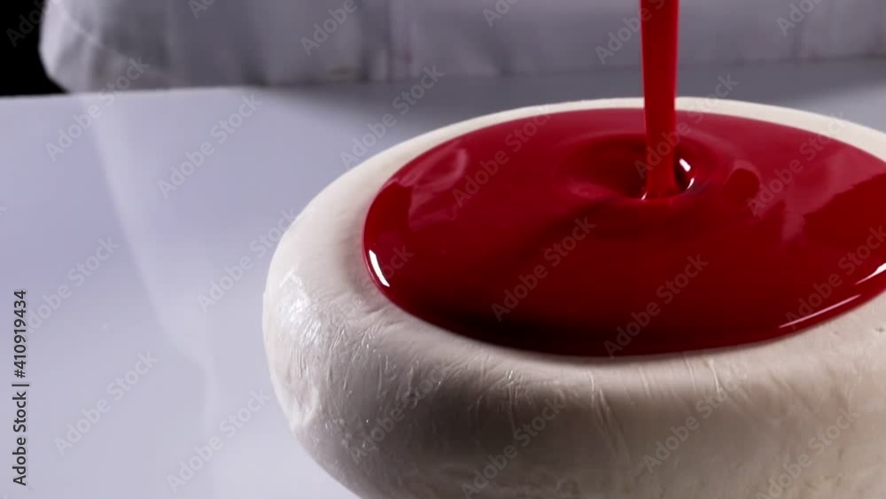 red mirror glaze is poured onto a round frozen mousse cake. The process ...