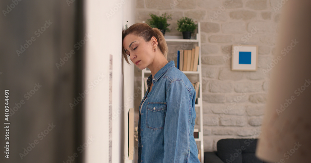 Young woman hits her head against the wall. The stressed young woman ...