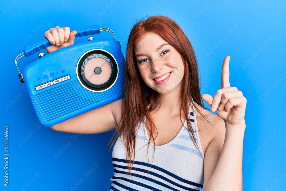 Young red head girl holding vintage radio smiling with an idea or ...