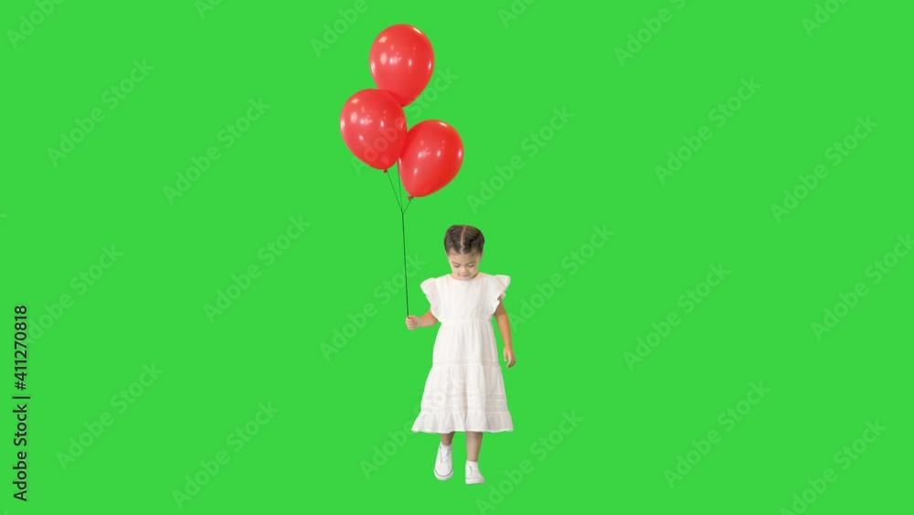 Adorable little girl holds tightly to a large bunch of helium balloons ...