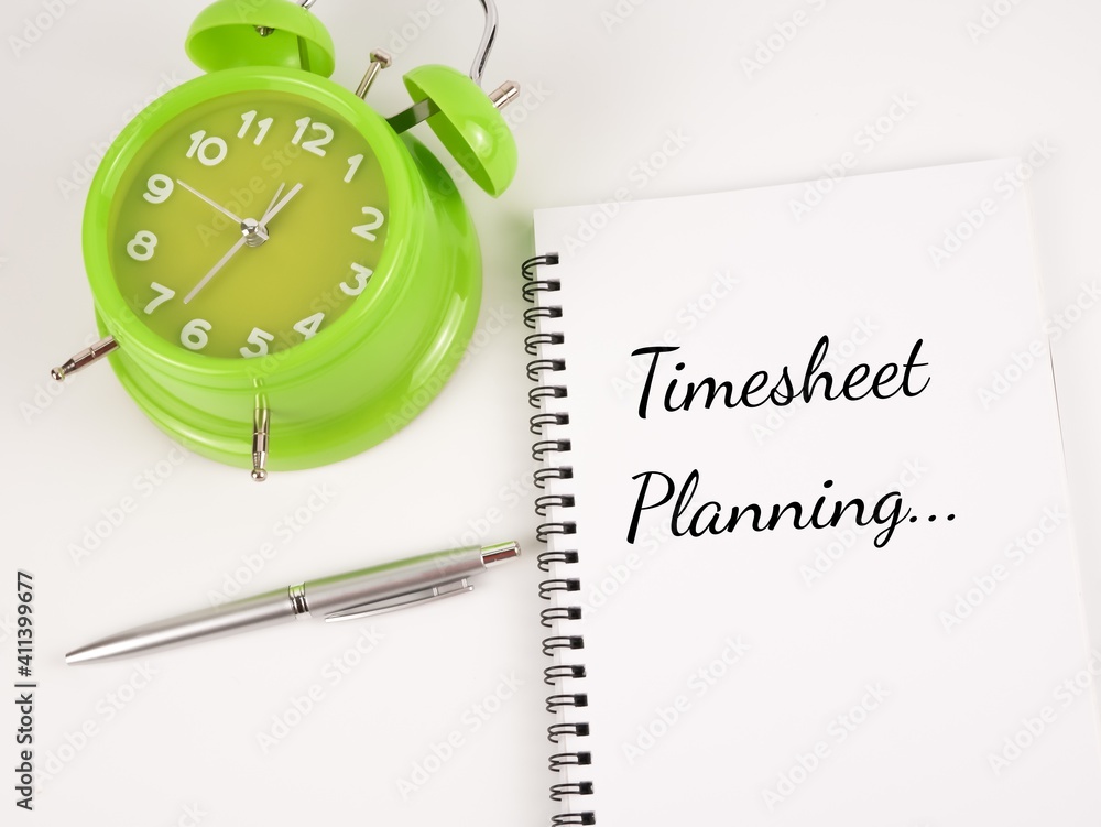 Top view of clock, pen and notebook written "Timesheet Planning ...