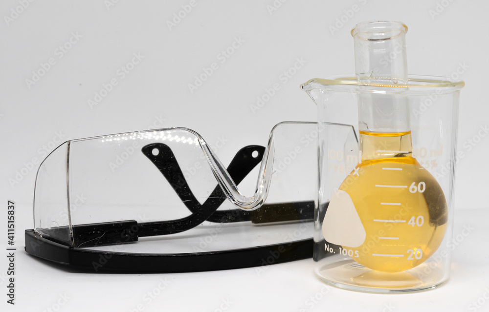 Yellow liquid in scintific beakers with safety glases and a white ...