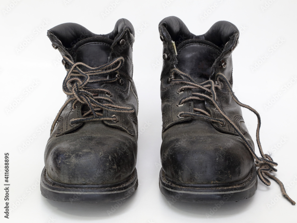 An pair of old, worn, black leather steel-toe work boots is shown in a ...