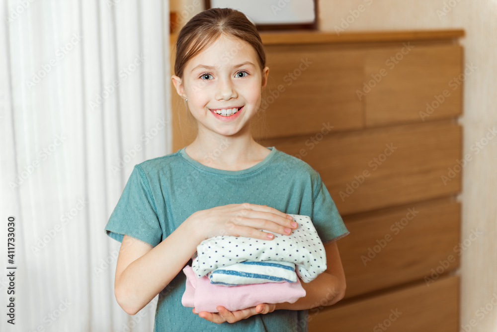 Happy cute girl puts things in order in the closet. A stack of colorful ...