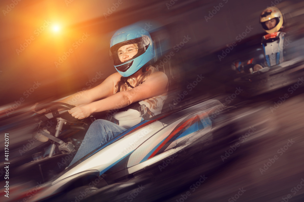 Glad cheerful positive girl and her friends competing on racing cars at ...