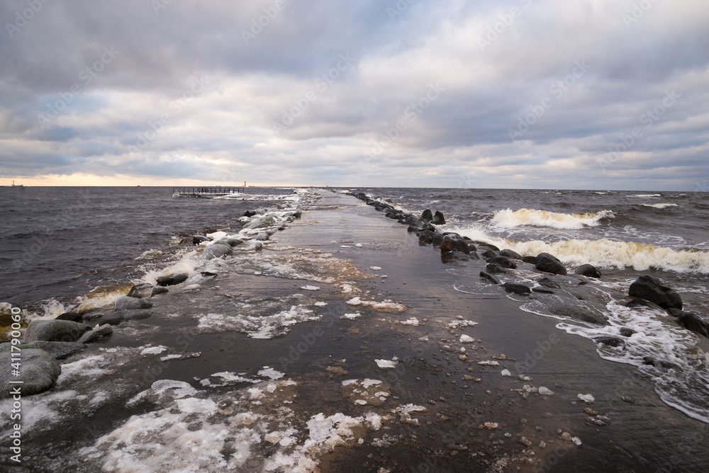 Landscape - a frozen pier in winter at sea with white foam waves in the ...