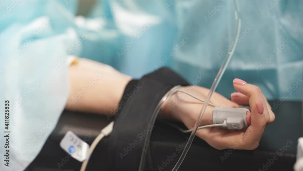 Close-up of a patient's hand with an IV lying on the operating table ...