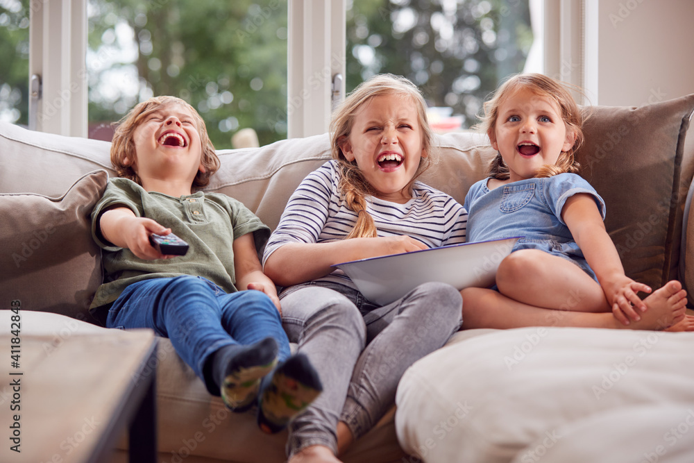 Three Children Sitting On Sofa At Home Laughing And Watching TV With ...