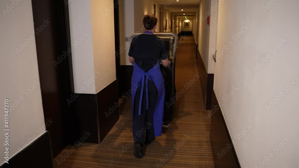Back view of female hotel room cleaner walking with cleaning trolley ...