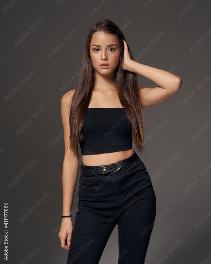 studio portrait of young slim tanned caucasian girl in black jeans and ...